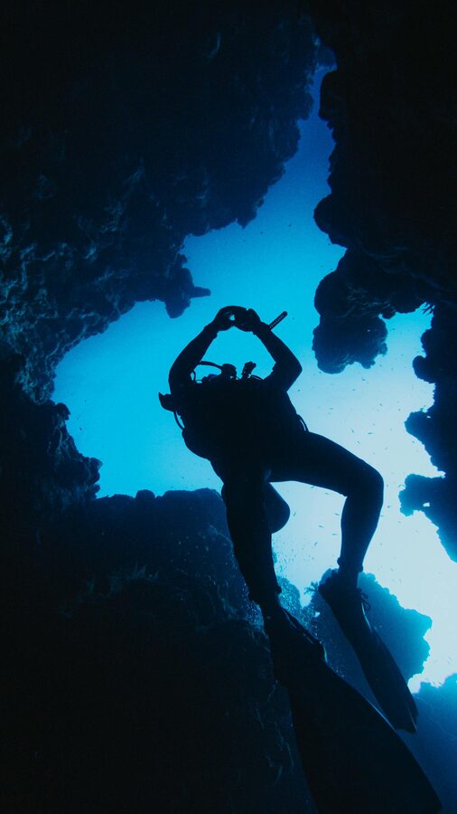 Scuba diver exploring an underwater cave formation with natural light filtering through