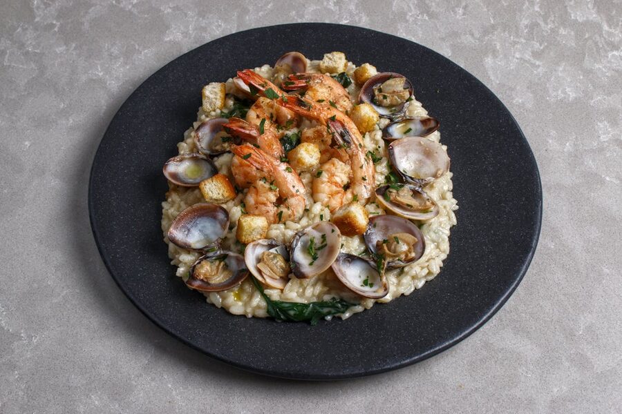 A gourmet seafood risotto topped with shrimp and clams served on a black plate
