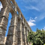 The Roman Aqueduct of Segovia rising against a clear blue sky, showing its massive stone arches