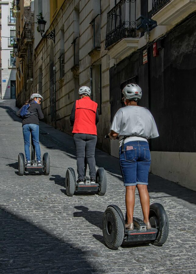 Three adults riding Segways up a cobblestone street in a Spanish city