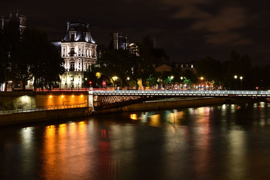 The Eiffel Tower lit up at night with reflections on the calm Seine River waters