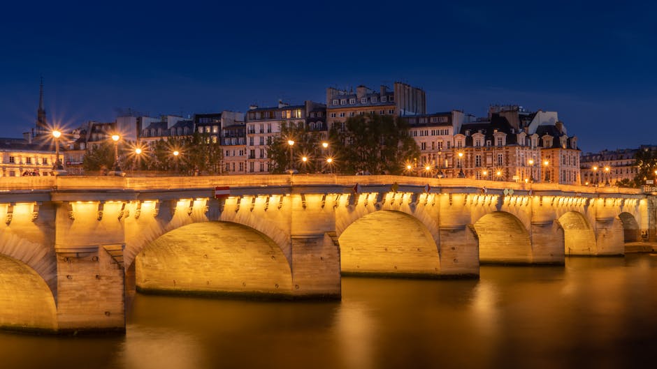 The historic Pont Neuf bridge illuminated at night with reflections on the Seine River