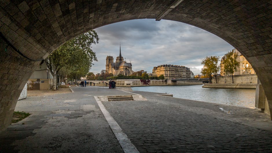 A view of Notre Dame Cathedral framed through a stone archway along the banks of the Seine River
