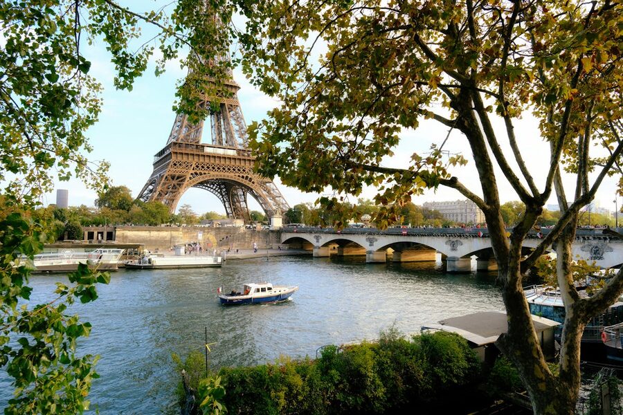 Eiffel Tower over the Seine River framed by lush green trees in summer