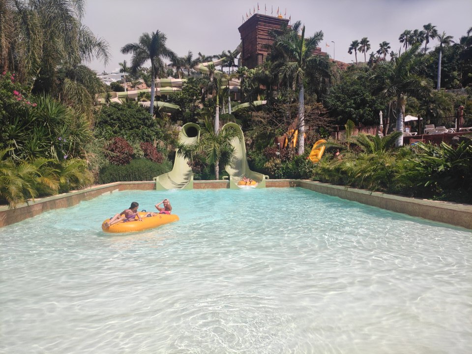 Wave pool area at Siam Park surrounded by palm trees and Thai structures