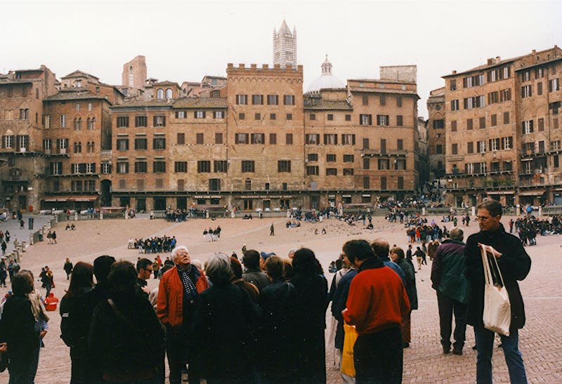 Tourists and locals gathering in Piazza del Campo Siena with medieval tower and buildings