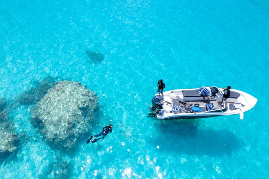 Snorkelers exploring clear turquoise waters near a boat from overhead