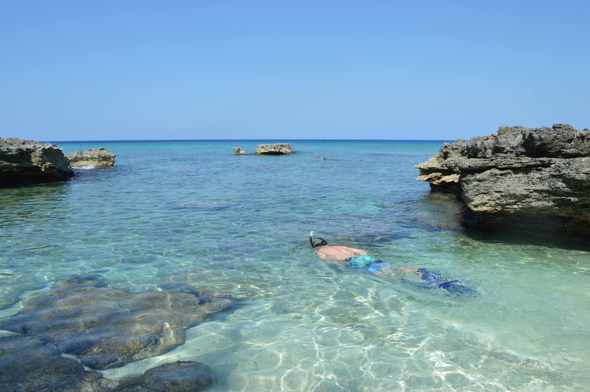 Person snorkeling in crystal clear tropical waters surrounded by rocky formations