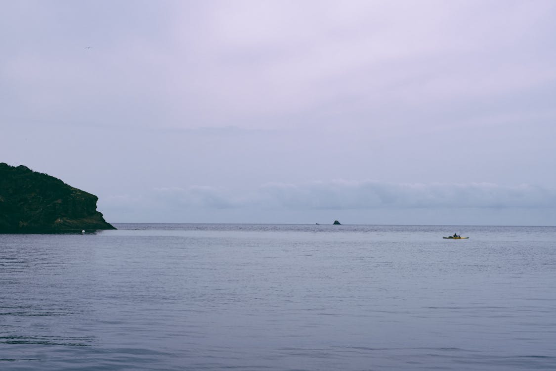 Lone kayaker on calm waters near a rugged cliff