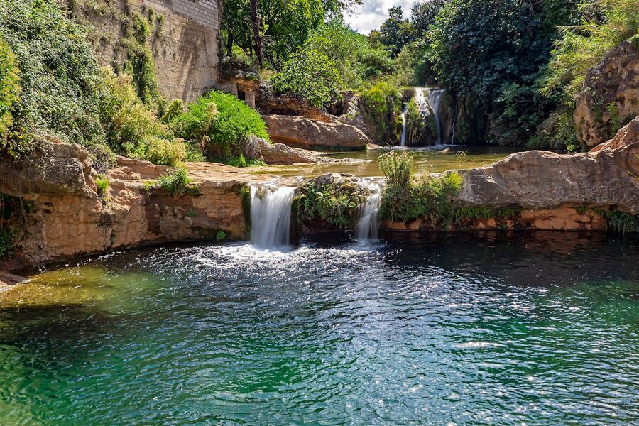 A waterfall cascading over moss-covered rocks in a forested mountain landscape in Spain