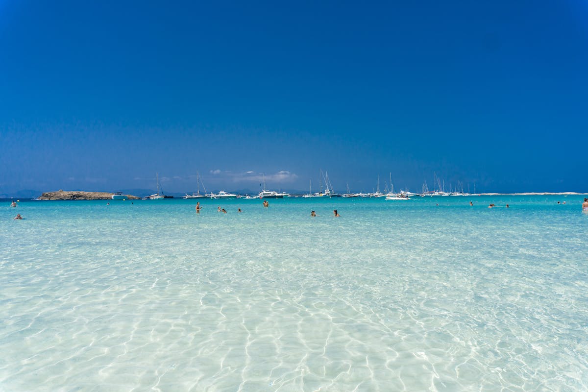 Leisure scene at a Spanish beach with turquoise waters and yachts in the distance
