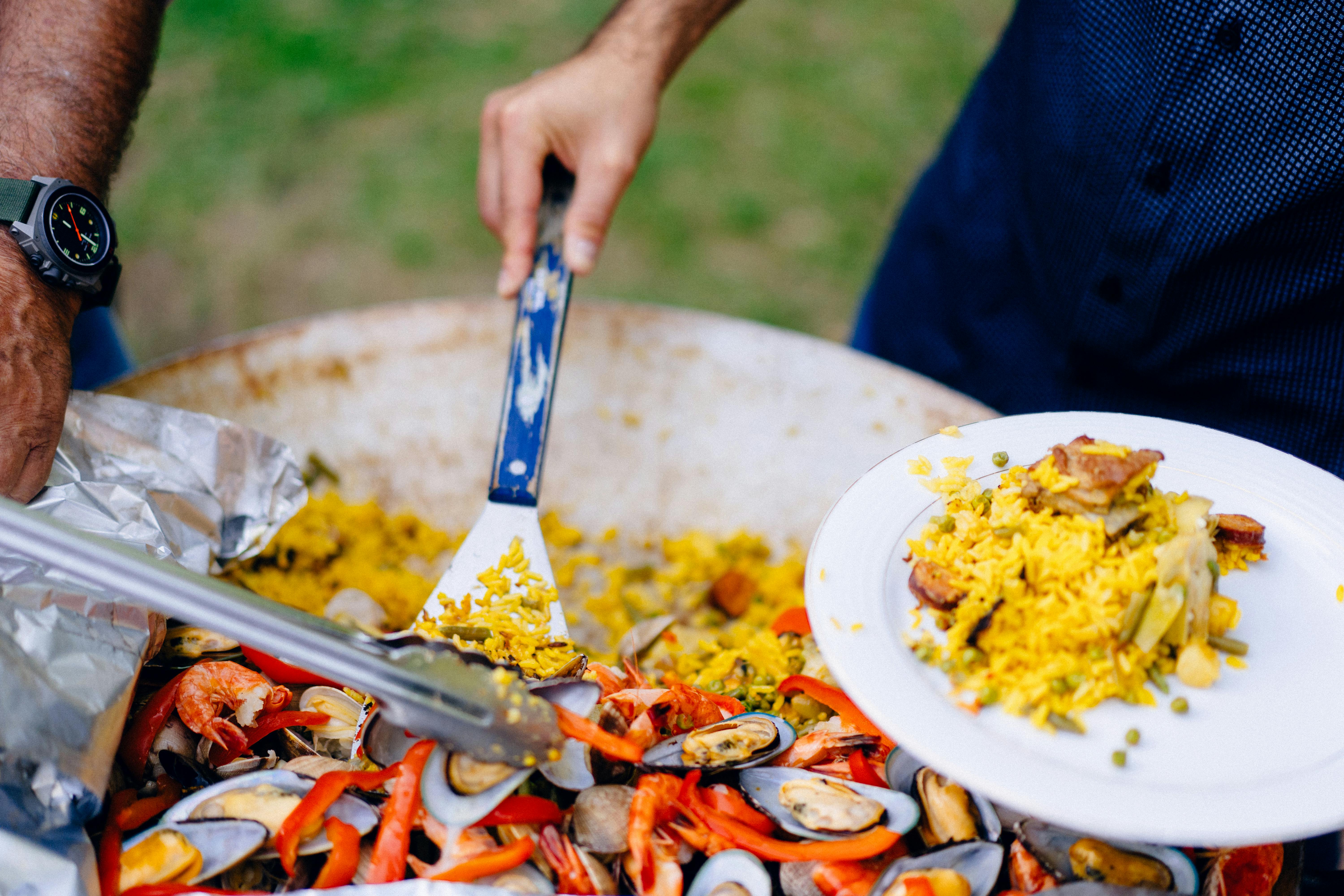 Hands serving Spanish paella with shrimp and mussels