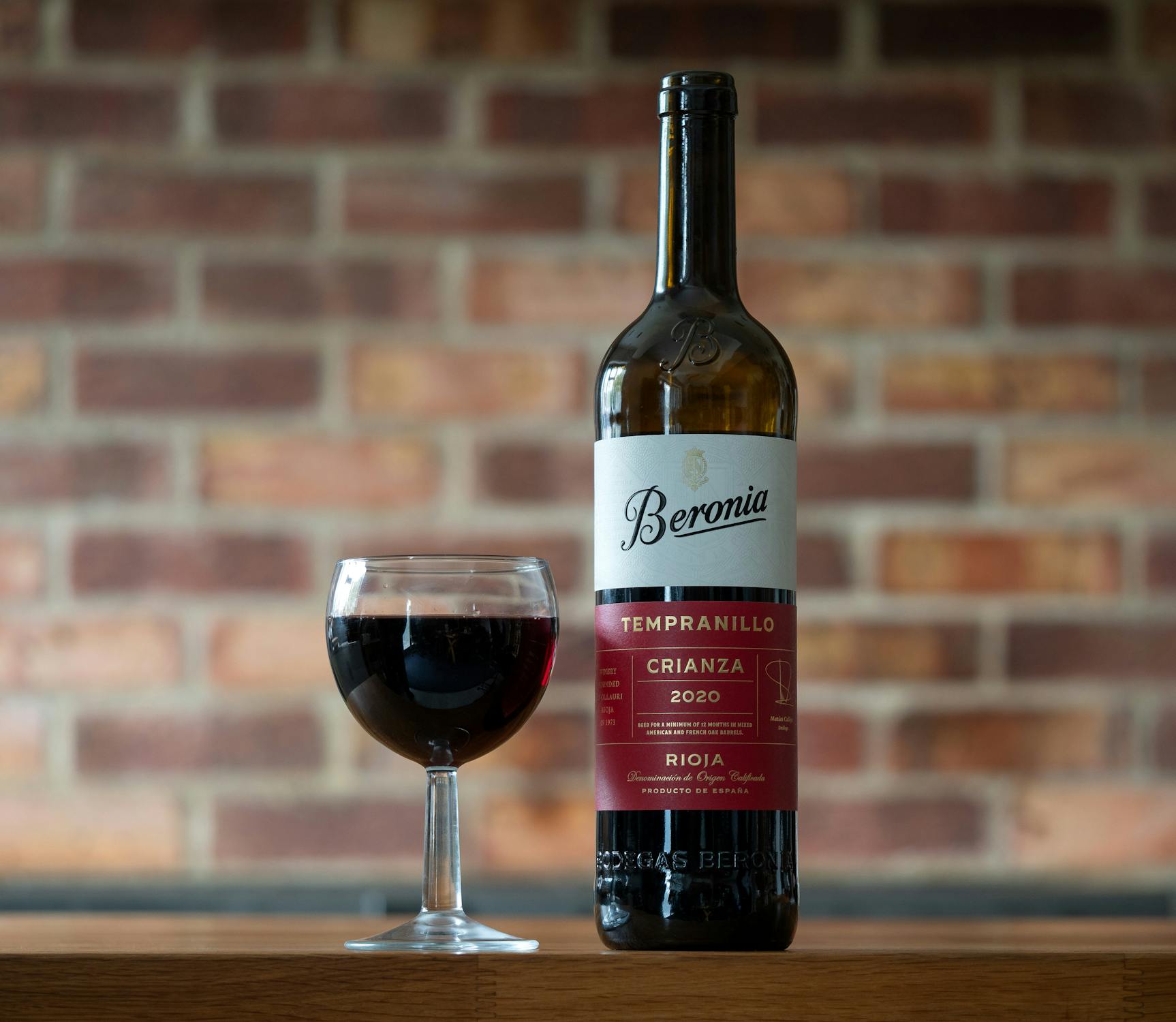 Spanish red wine bottle and glass against brick background
