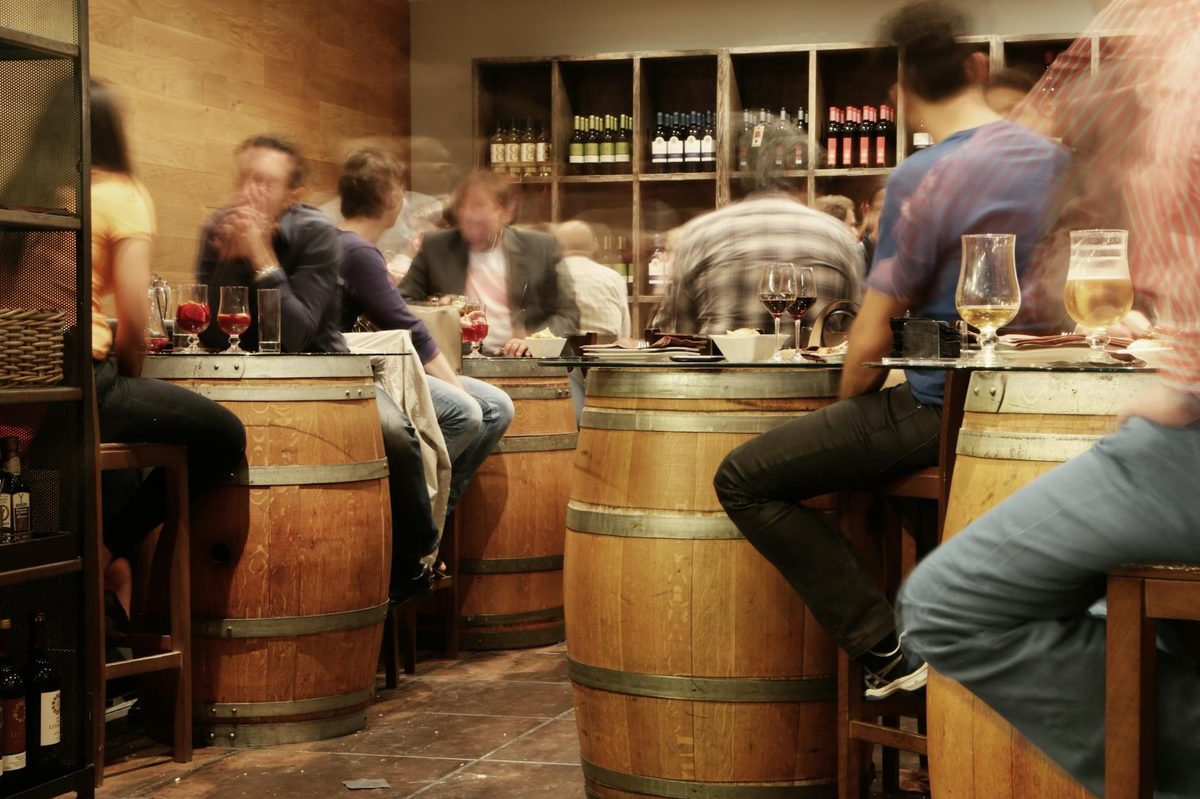 People enjoying drinks and tapas around wine barrel tables at a Spanish bar
