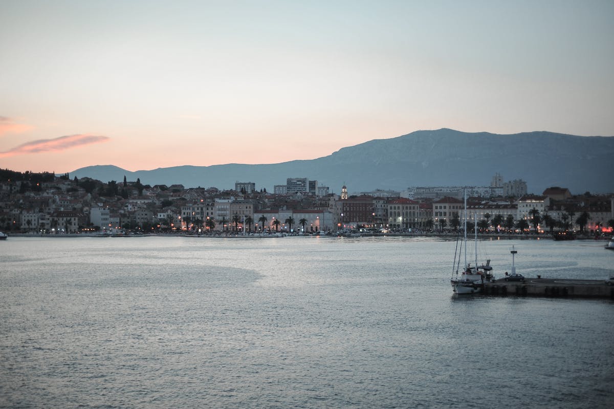 Split waterfront promenade with sailboat and mountain at sunset