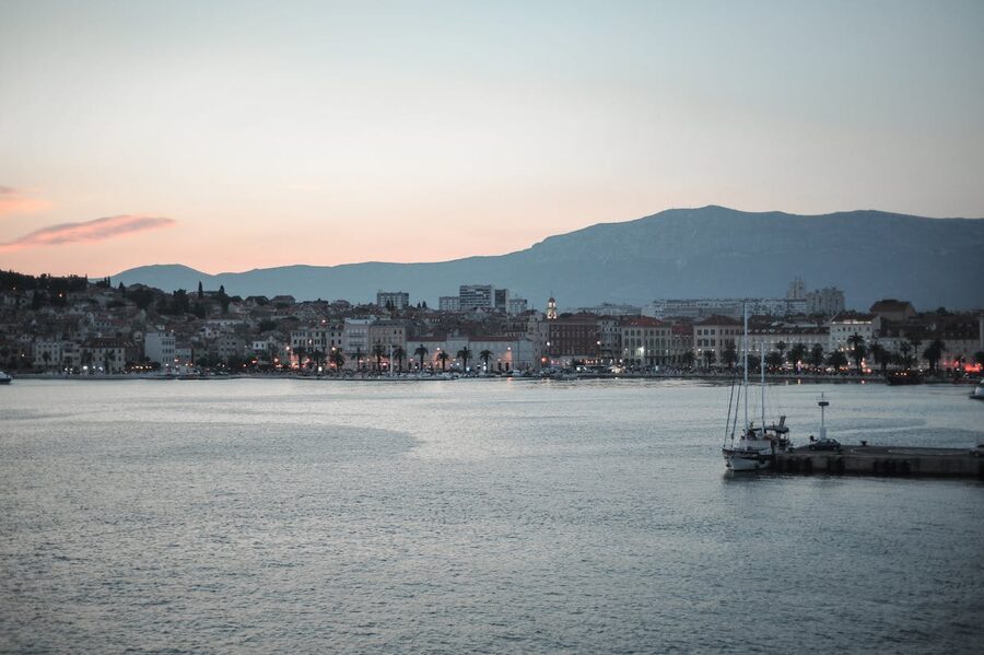 Split waterfront promenade with sailboat and mountain at sunset
