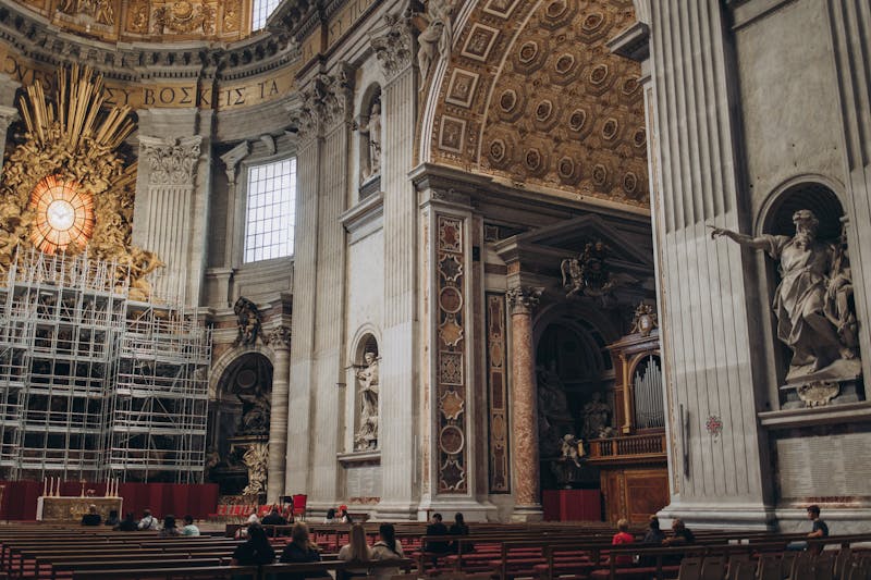 Interior nave of St. Peter's Basilica showing the ornate ceiling, marble floors, and visitors