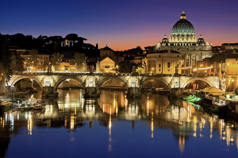 St Peters Basilica dome and Ponte Sant Angelo bridge illuminated at sunset over the Tiber River in Rome