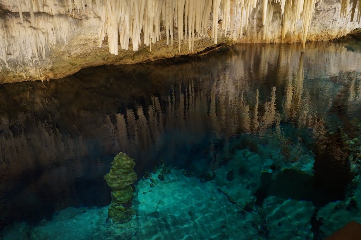 Stalactites hanging from cave ceiling over a crystal clear underground lake