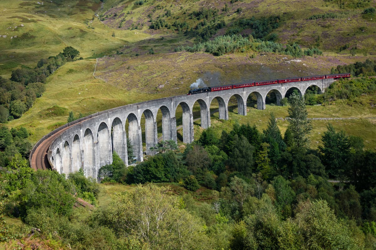 A steam train crossing the Glenfinnan Viaduct through the Scottish countryside