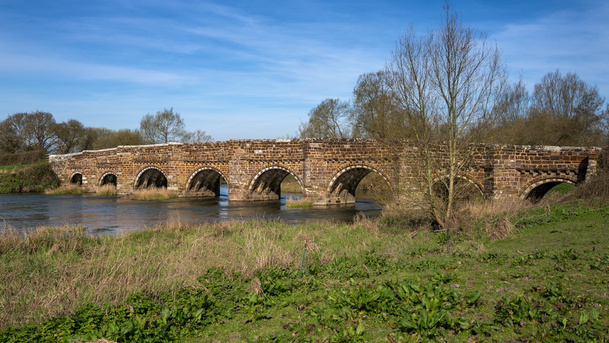 Historic stone bridge crossing a river in the English countryside with lush green surroundings