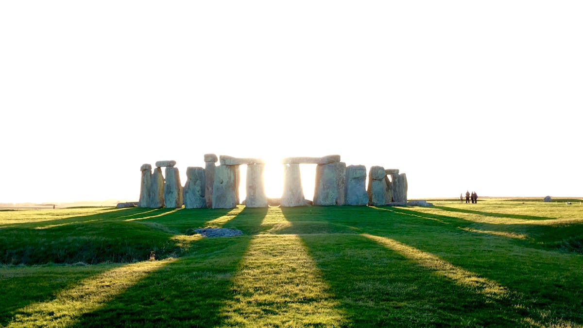 Stonehenge stones casting long shadows across green grass in sunlight
