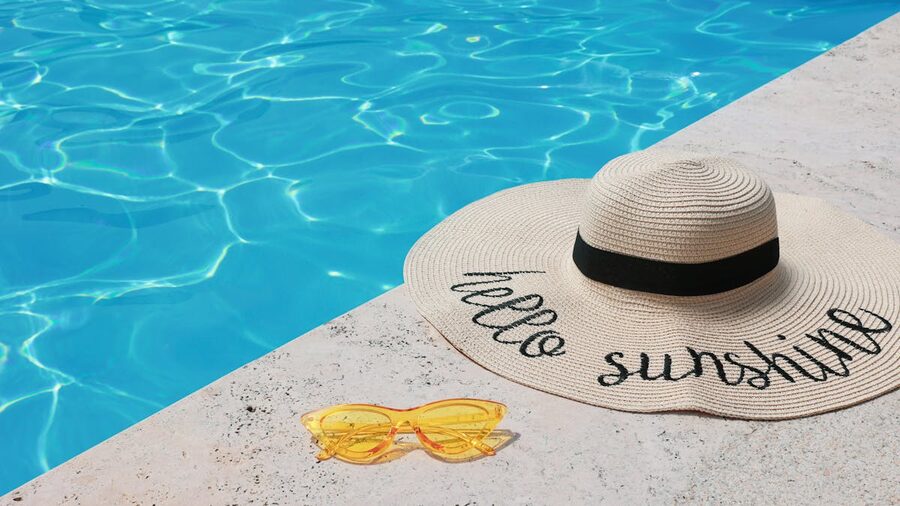 Elegant straw hat and yellow sunglasses beside a shimmering pool embodying summer
