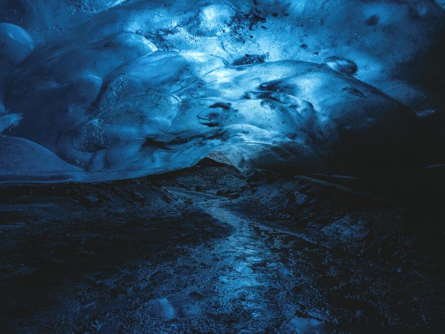 Striking image of a blue ice cave with a river flowing beneath, capturing a surreal winter ambiance.