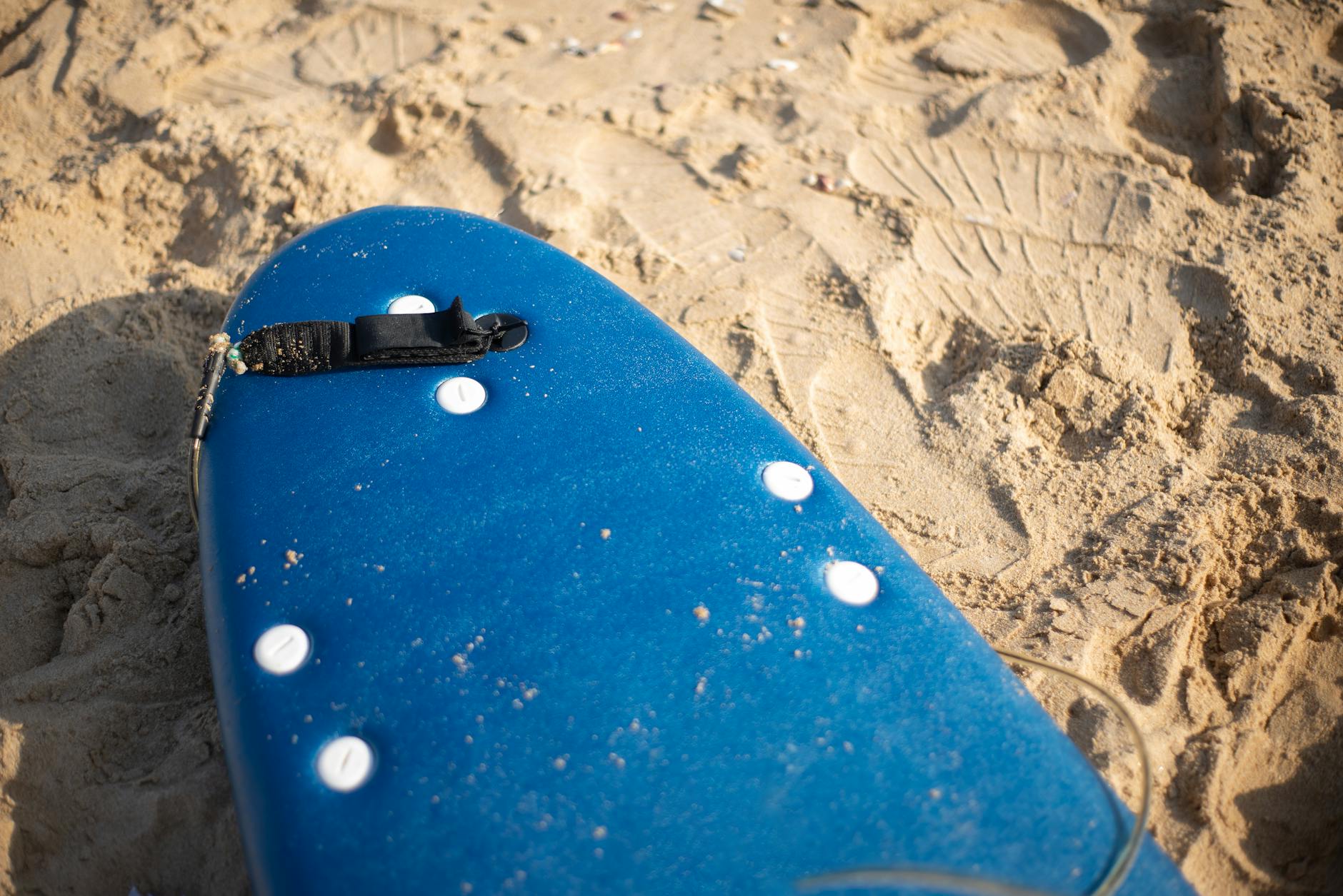 Close-up of a blue surfboard resting on the sandy beach