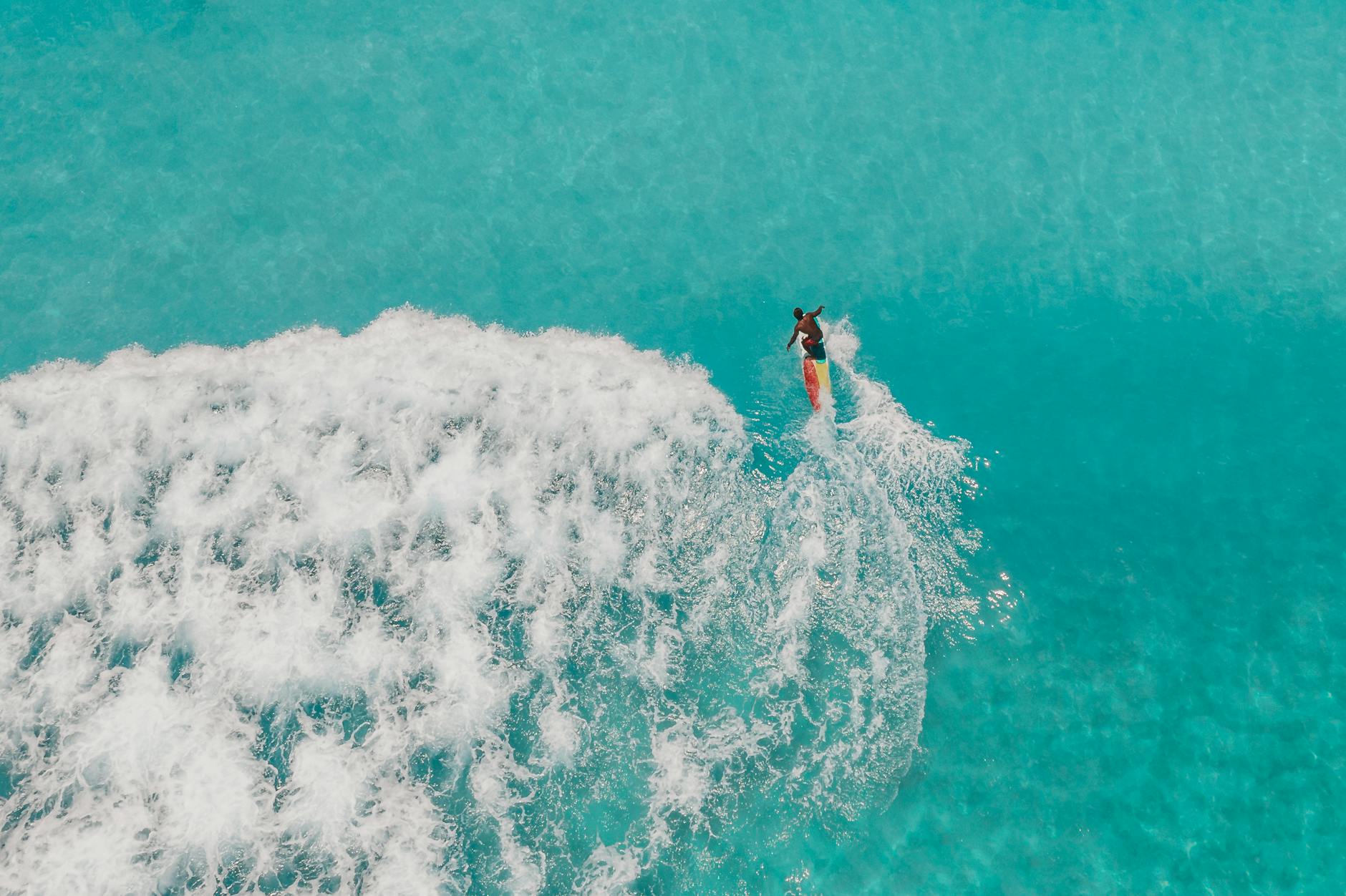 A surfer rides a turquoise wave captured from above