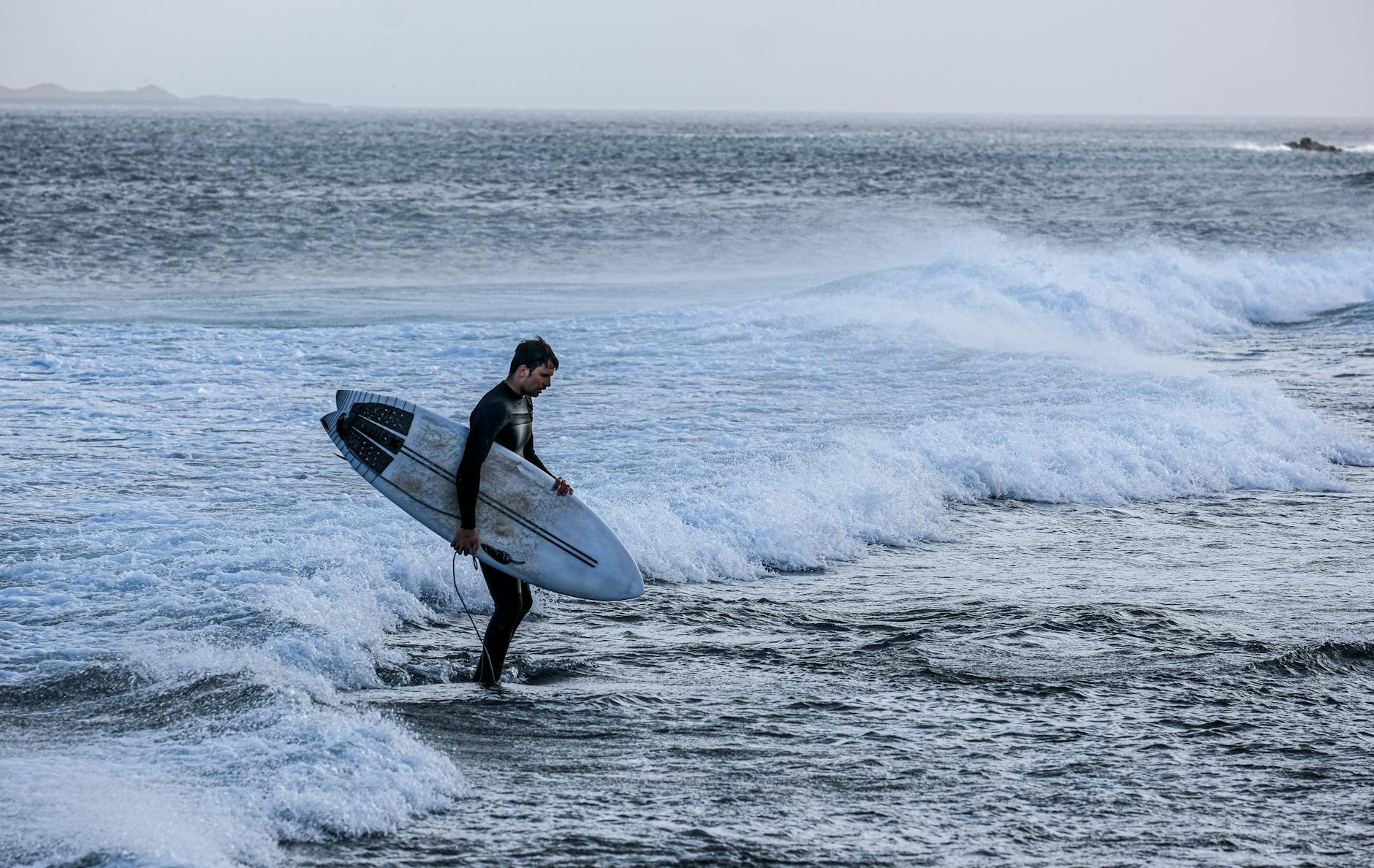 A surfer carrying a board walks into the ocean waves