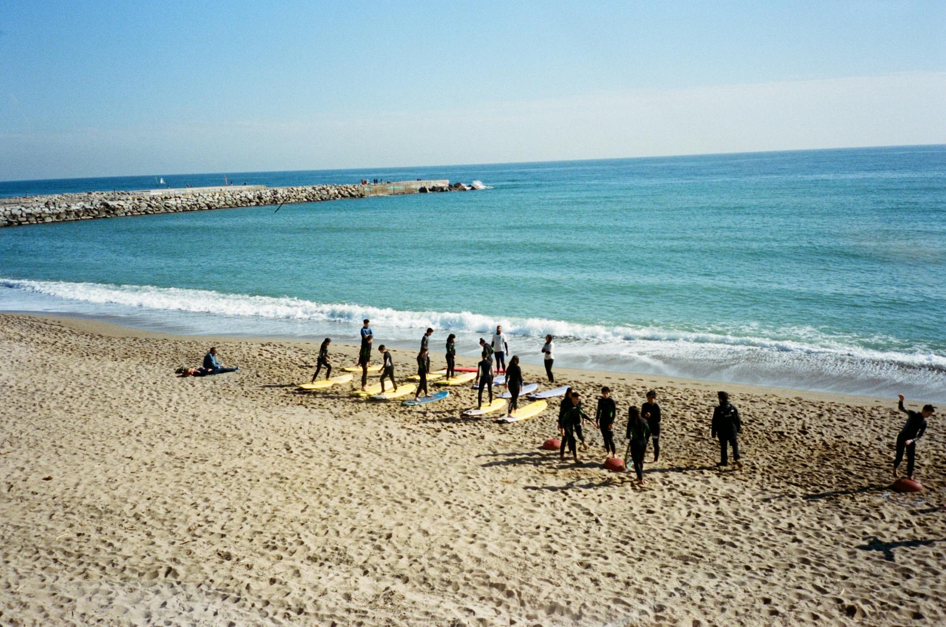 A group of surfers in wetsuits practicing on surfboards at a sunny beach