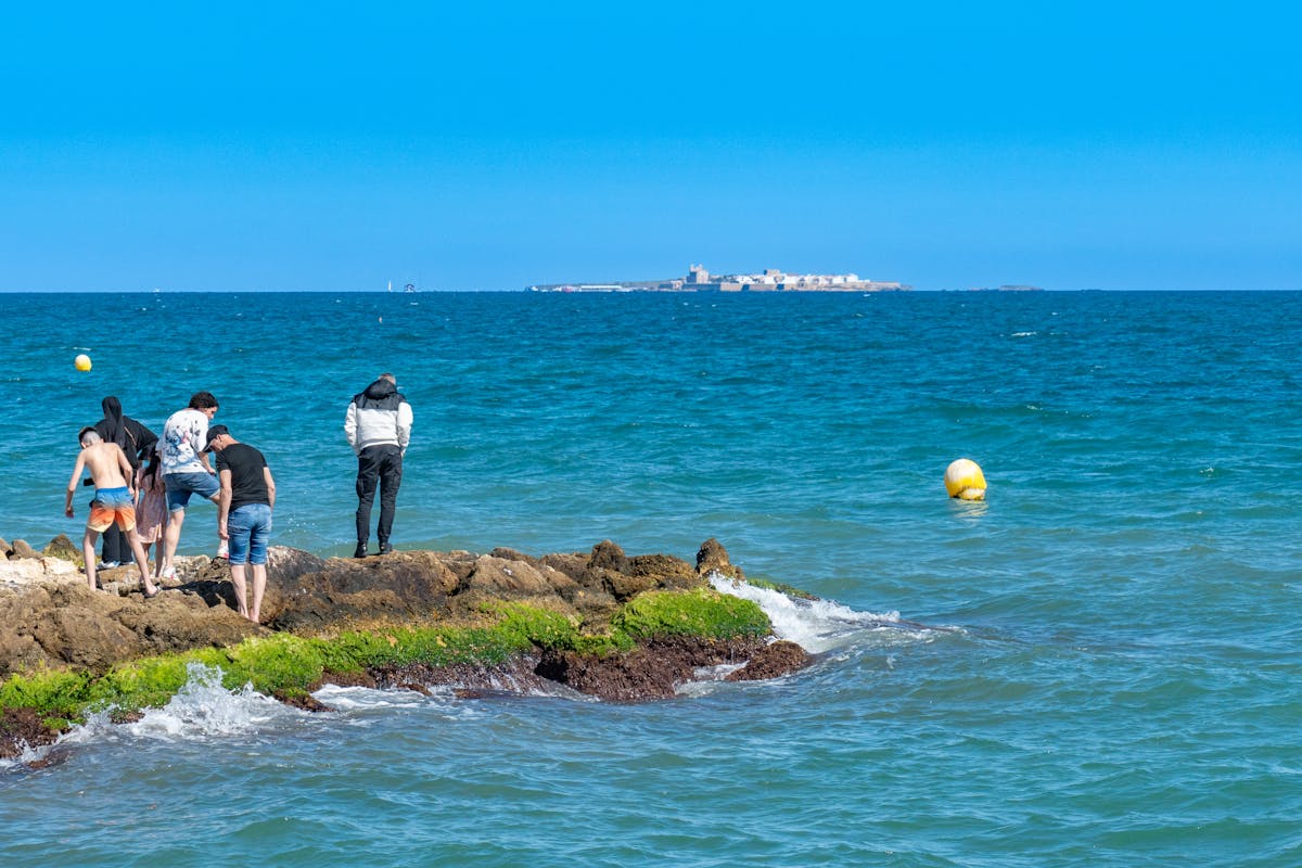 People standing on rocky shore at Santa Pola Spain with island visible in distance