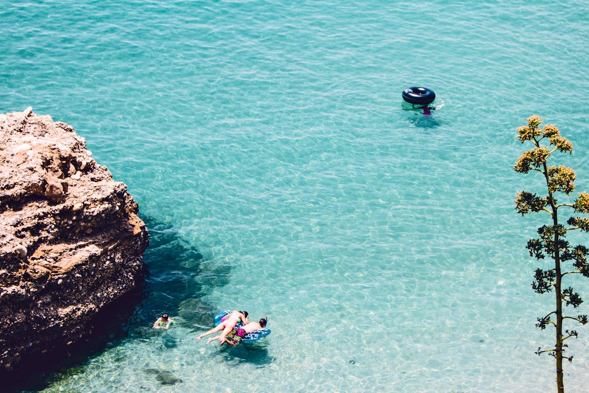 People swimming in clear blue Mediterranean water near a rocky coastline