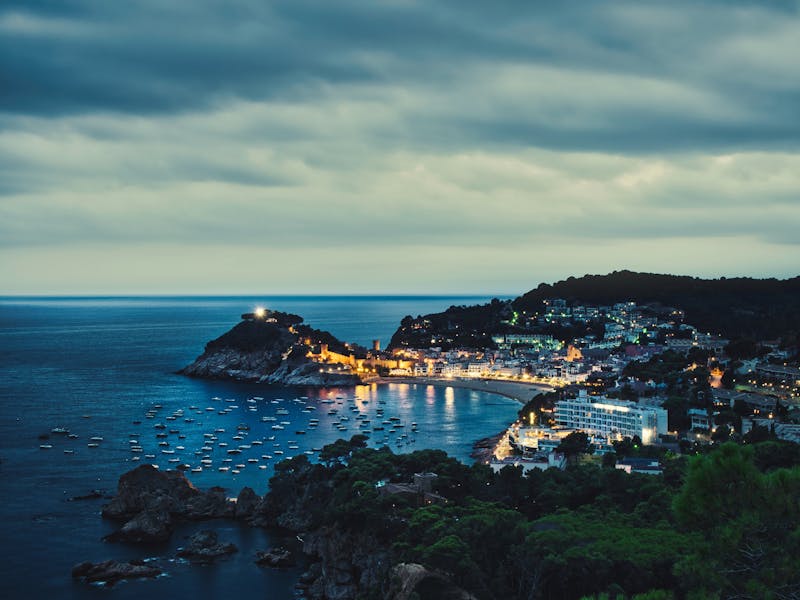 Illuminated waterfront of Tamariu fishing village at dusk with boats in the bay
