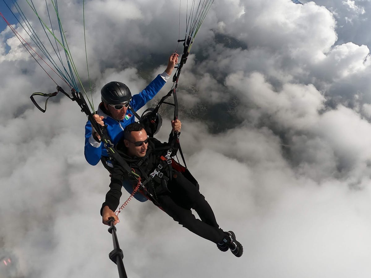 Two people tandem paragliding above the clouds