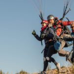 Two paragliders running for takeoff on a grassy hillside
