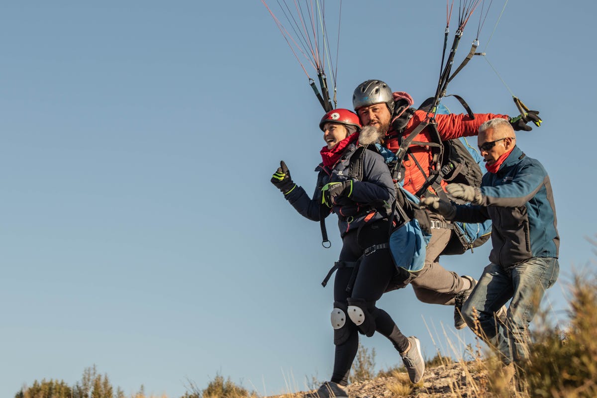 Two paragliders running for takeoff on a grassy hillside
