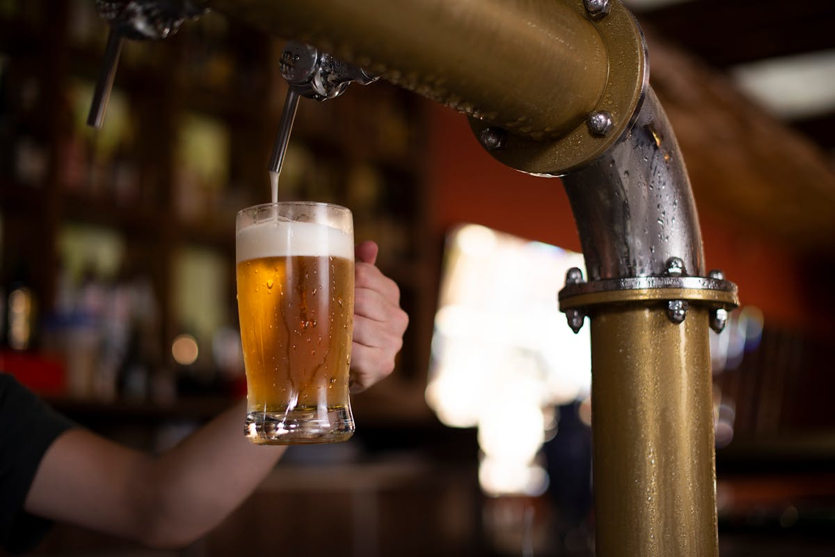 Close-up of a hand holding a mug as beer is poured from a brewery tap
