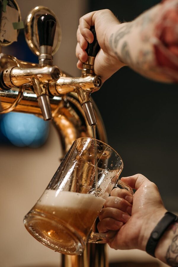 Close-up of a hand holding a mug as beer is poured from a brewery tap