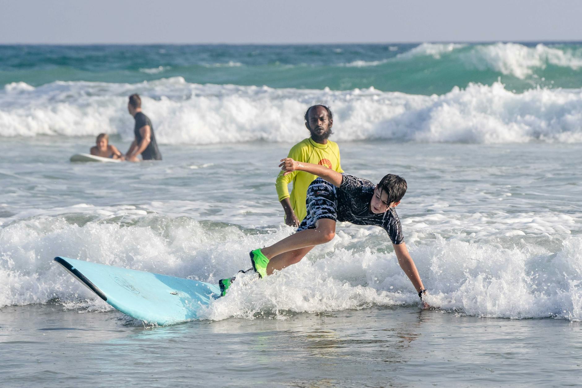A teenager learning to surf with an instructor in a sunny beach setting