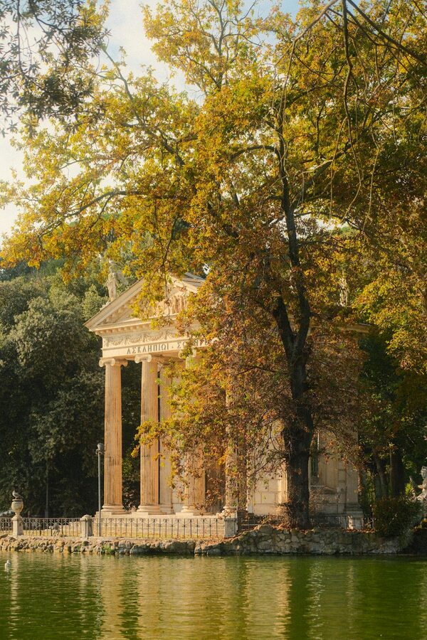 Temple of Aesculapius reflected in the lake surrounded by autumn leaves in Villa Borghese Rome