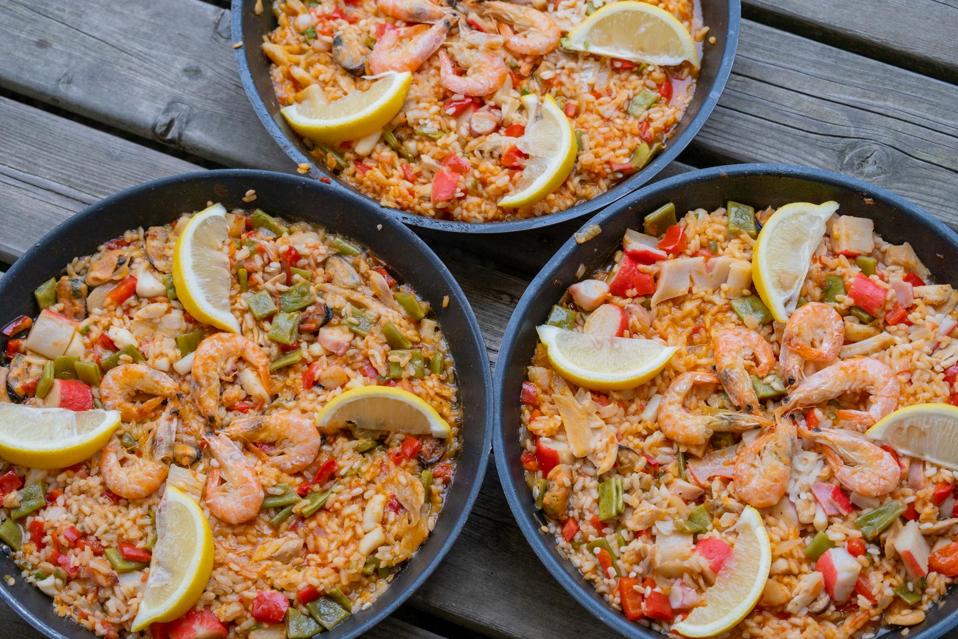 Three pans of seafood paella with lemon slices on a wooden table