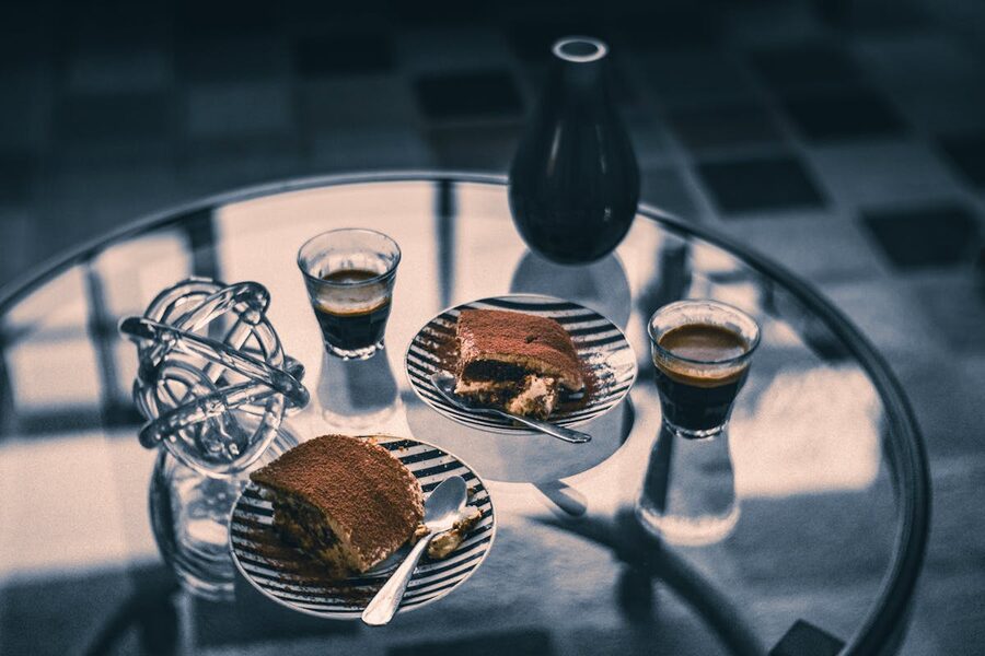 Tiramisu slices and espresso cups on a glass table in an Italian setting