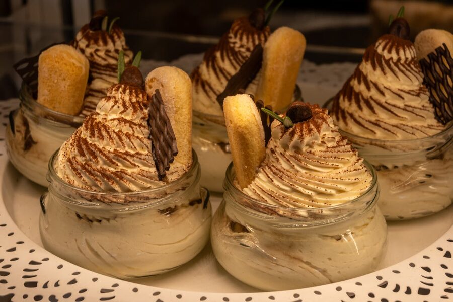 Tiramisu desserts served in glass jars topped with chocolate and ladyfinger biscuits