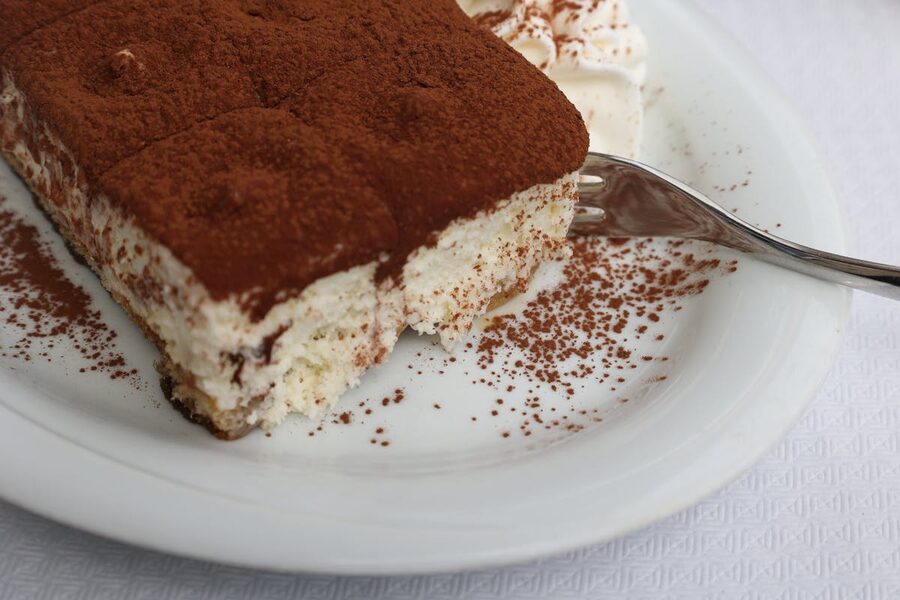 A slice of tiramisu covered in cocoa powder on a white plate