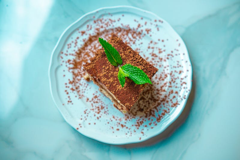 A slice of tiramisu garnished with fresh mint on a marble plate