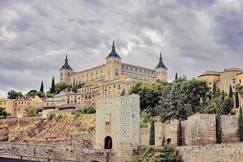 The Alcazar of Toledo rising above city walls under dramatic clouds