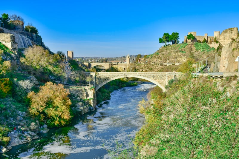 Historic stone bridge crossing the Tagus River in Toledo Spain with medieval walls in the background