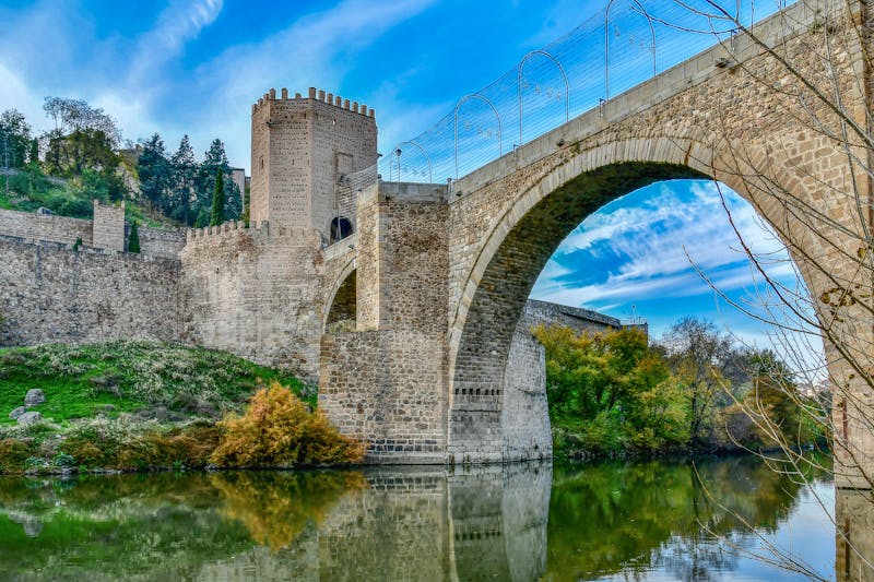 San Martin Bridge in Toledo Spain with autumn colors and clear blue sky reflection in the Tagus River